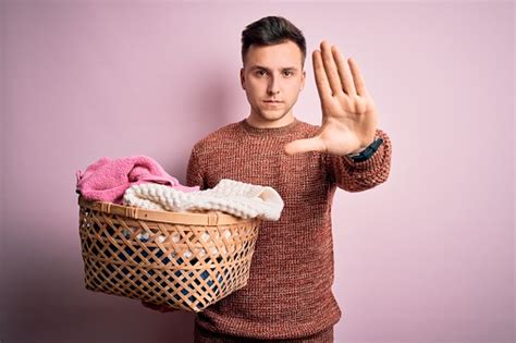 젊은 잘 생긴 백인 남자 하 고 집안일 집안일 들고 빨래 고리 버들 바구니와 오픈 손으로 정지 기호와 심각 하 고 자신감 있는 표정 방어 제스처 가사 집안일에 대한 스톡
