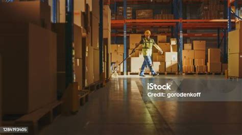 작업자는 손 팔레트 트럭을 사용하여 골판지 상자를 이동 소매 창고에서 상품과 선반의 행 사이를 걷고 사람들은 제품 유통 물류 센터에서 일합니다 사이드 뷰 샷 20 24세에