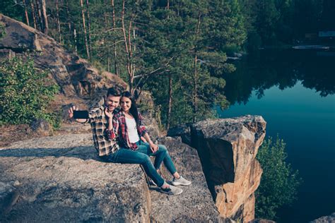 사랑 스러운 좋은 사랑 스러운 배우자 신혼 여행 입고 캐주얼 체크 무늬 셔츠와 청바지 바위 위에 앉아 만들기 Selfie 로맨틱 저녁 야생 나무 조 경 강에 대한 스톡 사진