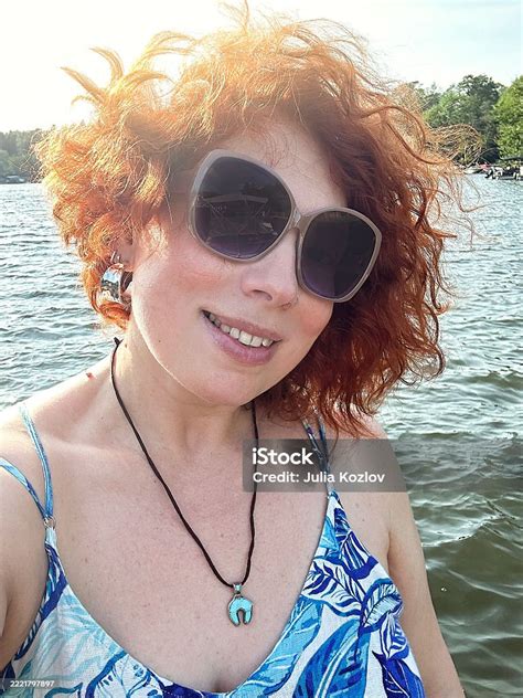 호숫가에서 웃고 있는 빨간 머리 여자 선글라스와 블루 패턴의 탑을 착용한 휴가 셀카 45 49세에 대한 스톡 사진 및 기타 이미지 45 49세 곱슬 머리 관광
