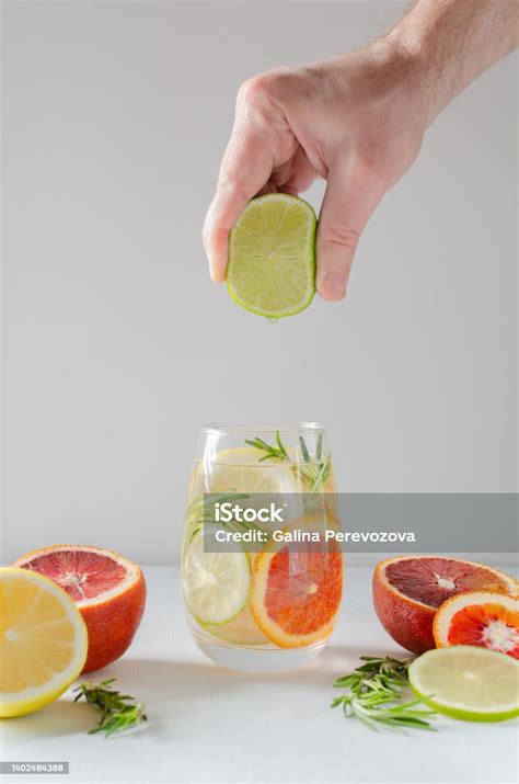 레몬 라임 레드 오렌지 로즈마리가 들어간 유리에 미네랄이 주입 된 물 유리에 라임을 쥐어 짜내는 손 감귤류 과일에 대한 스톡 사진 및 기타 이미지 Istock