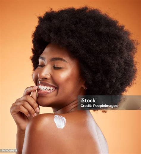 크림 스킨케어 흑인 여성은 주황색 스튜디오 배경을 배경으로 몸을 위한 제품에 대해 흥분했습니다 젊고 행복하며 아프리카 모델의