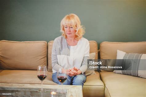 누군가를 기다리는 레드 와인 두 잔과 함께 소파에 앉아 있는 중년 금발 머리 슬픈 여자 외로움 싸움 축하 혼자 개념 가정 생활에 대한 스톡 사진 및 기타 이미지 Istock