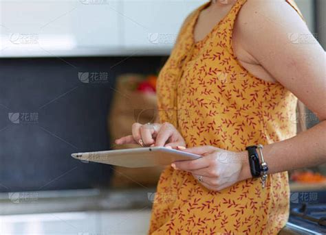 厨房里年轻迷人的高加索黑发家庭主妇的画像早上喝一杯咖啡和平板电脑