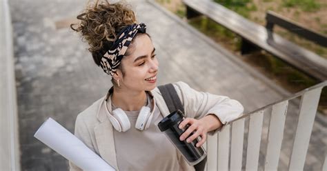 한 여성 젊은 성인 백인 여학생이 배낭을 메고 대학 건물 앞에 서서 종이와 커피 한 잔을 들고 밝은 날에 야외에서 행복한 미소를 지으며 실제 사람들이 공간을 복사한다 사진