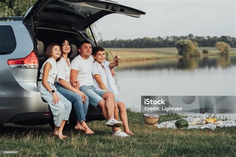 미니밴 자동차 트렁크에 앉아있는 행복한 네 명의 백인 구성원 가족 십대 자녀 두 명과 함께 어머니와 아버지 호수 옆에서 주말 피크닉을하는 아들과 딸이 4 명에 대한 스톡
