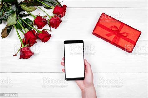 여성의 손에 빈 화면 흰색 배경에 장미와 선물 상자의 꽃다발 복사 공간 모바일 스마트 폰 발렌타인 데이 여성의 날 어머니의 날 상단 보기 플랫 레이 발렌타인 카드에 대한