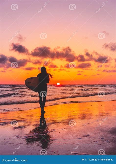 Silhouette Of The Surfer Girl With Surfboard On A Beach At Sunset