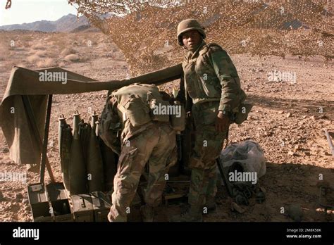 Two Gun Crewmen In Front Of A Stand Of 155 Mm Projectiles Including M107 High Explosive