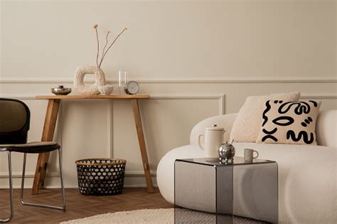 하얀 소파 유리 커피 테이블 나무 벤치 말린 꽃이 있는 베이지색 꽃병 무늬가 있는 베개 검은색 의자 및 개인 액세서리가 있는 거실 인테리어의 아늑한 구성 가정 장식 템플렛