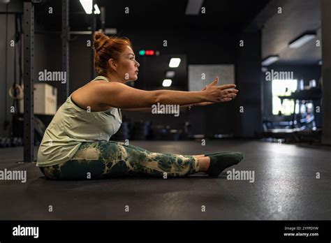 Athletic Redhead Woman Performing Stretching Routine In Contemporary Fitness Facility Full Body