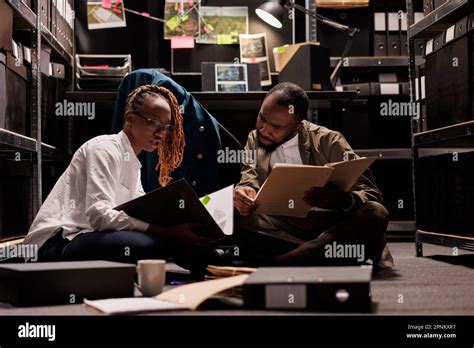 Policewoman Showing Colleague Crime Case File Information While Analyzing Records At Night Time