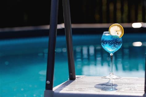 수영장 배경에 맛있는 파란색 칵테일 블루 라군과 노란색 레몬 한 잔 알콜 칵테일 육즙이 많은 과일 블루와 Curacao 리큐어 아이스 큐브 및 레몬 조각 0명에 대한 스톡