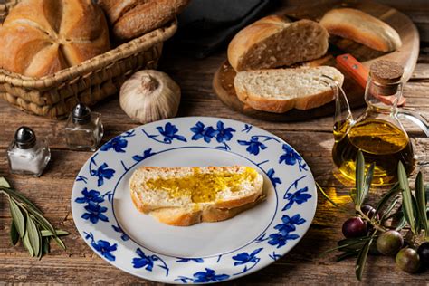 더 많은 조각 기름 캔 마늘 올리브가 든 가지 소금 후추 빵이 든 빵 바구니 소박한 배경이 있는 도마 옆 접시에 올리브 오일을 곁들인 빵 조각 0명에 대한 스톡 사진 및