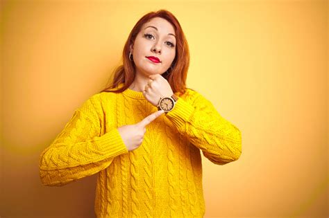 아름다운 빨간 머리 여자 착용 겨울 스웨터 위에 서 고립 된 노란색 배경 에 서 서둘러 가리키는 시계 시간 조바심 편안한