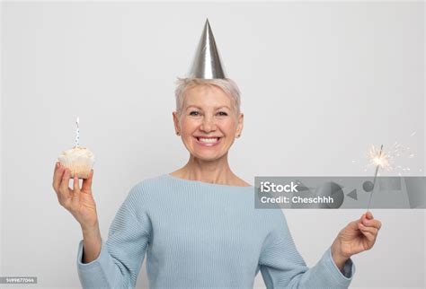 촛불과 스파클러와 컵 케이크와 함께 생일을 축하하는 원뿔 모자를 쓰고 있는 행복한 중년 여성 60 64세에 대한 스톡 사진 및 기타 이미지 Istock
