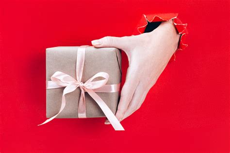 빨간 배경의 구멍을 통해 분홍색 리본공예 종이에 싸여 선물 상자를 들고 여성 손 2020년에 대한 스톡 사진 및 기타 이미지