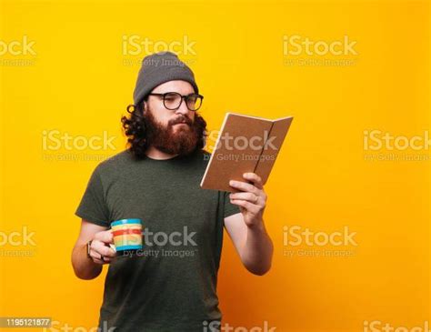 녹색 티셔츠를 입고 안경과 모자를 쓰고 책을 읽고 커피 한 잔을 들고 있는 수염난 힙스터 남자 책에 대한 스톡 사진 및 기타