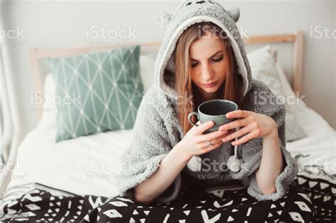 젊은 아름 다운 여자 침대에서 집에서 휴식 재미 회색 후드를 입고 게으른 주말 아침 차 또는 커피 한잔과 함께 놀 아 요 가정 생활에 대한 스톡 사진 및 기타 이미지