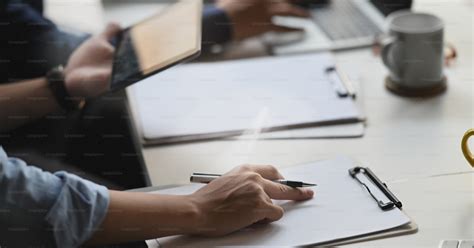 클립보드와 커피잔으로 둘러싸인 흰색 작업 책상에 앉아 컴퓨터 노트북과 태블릿으로 함께 작업하는 비즈니스 개발자 팀의 잘린 이미지