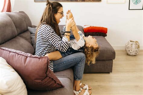 Madre con la boca abierta cogiendo las manos de su hija juguetona mientras está sentada con ella