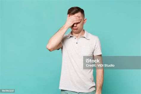 파란 청록색 벽 배경에 고립 된 손바닥으로 눈을 덮고 캐주얼 복장에 기분을 상하게 젊은 남자의 초상화 사람들은 진심으로 감정