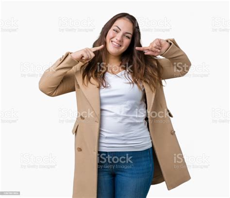 플러스 크기 젊은 여 자가 아름 다운 미소를 보여주는 자신감과 손가락 치아와 입 지적 배경 고립에 겨울 코트를 입고 건강 개념입니다 가리키기에 대한 스톡 사진 및 기타