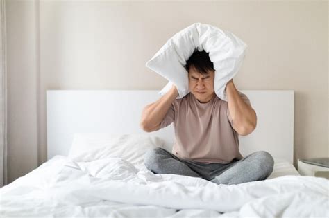 Premium Photo Unhappy Asian Man Sitting On Bed Covering Head With Pillow