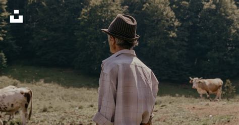 검은 페도라 모자를 쓰고 갈색 및 흰색 격자 무늬 드레스 셔츠를 입은 남자가 푸른 잔디에 서 있다 사진 Unsplash의