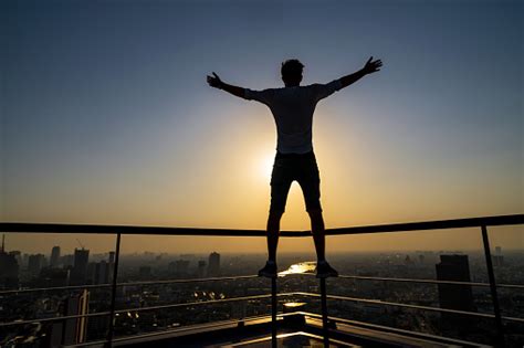 렌즈 플레어 라이프 스타일 및 자유 개념 일몰 시간에서 도시 배경 위에 확장 팔 동작으로 서 남자의 실루엣 개념에 대한 스톡 사진 및 기타 이미지 Istock