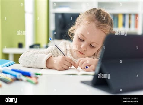 Adorable Blonde Girl Student Using Touchpad Writing On Notebook At