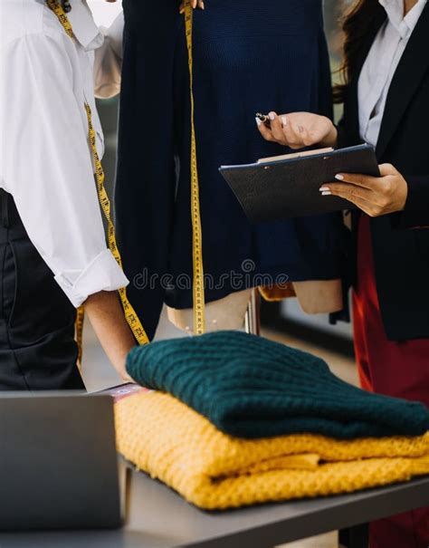 Female Fashion Designer Looking At Drawings And Sketches That Are Pinned To The Wall Behind