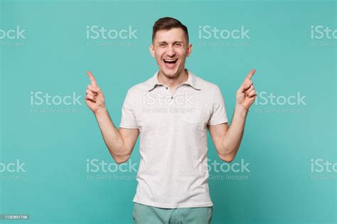 캐주얼에서 쾌활 한 젊은 남자의 초상화를 가리키는 인덱스 손가락 옆에 파란색 청록색 벽 배경에 고립 스튜디오 사람들은 진심으로 감정 라이프 스타일 개념입니다 복사 공간을