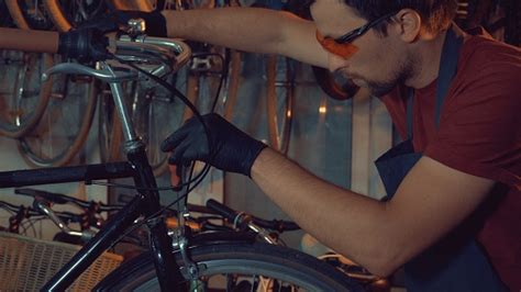 테마 중소 기업 자전거 수리 보호 안경 장갑과 Fartuhe에 젊은 갈색 머리 백인 남자는 수리 및 차고 작업장에서 림 브레이크와 바퀴 회전 자전거를 튜닝하기 위해 손