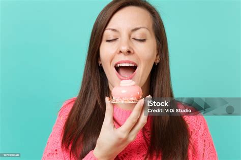 폐쇄 눈 뜬된 분홍색 스웨터에 아름 다운 젊은 여자 보유 손 블루 터키석 벽 배경 스튜디오 초상화에 고립 된 케이크를 먹는
