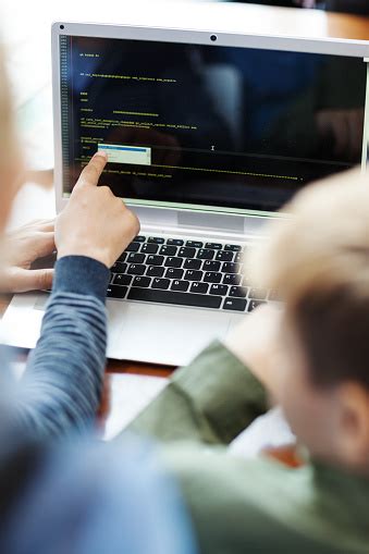 노트북 컴퓨터에서 코딩하는 방법을 배우는 두 명의 인식 할 수없는 학교 아이들의 어깨 너머로 한 소년이 화면의 메뉴를 가리킵니다 노트북에 대한 스톡 사진 및 기타 이미지