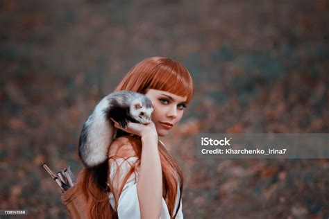 매력적인 레이디 장난과 유혹 카메라 불타는 붉은 머리와 앞 머리와 소녀는 손에 귀여운 길 들인 흰 족제비를 보유 그녀의 뒤에 화살의 화살을 가진 매력적인 열정적 인 사냥꾼