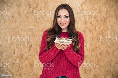 달콤한 여자 학생 캐주얼 옷 빛나는 햄 샌드위치와 그녀의 두 손으로 치즈를 보유 하 고 미소 생각 패스트 푸드 및 스낵의 건강에 유해 하지 않습니다 적절 하 고 건강 한