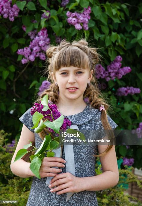 아름다운 머리띠를 가진 어린 소녀가 그녀의 손에 라일락 꽃을 들고 피는 나무 옆에 서 있습니다 8 9 살에 대한 스톡 사진 및 기타 이미지 Istock