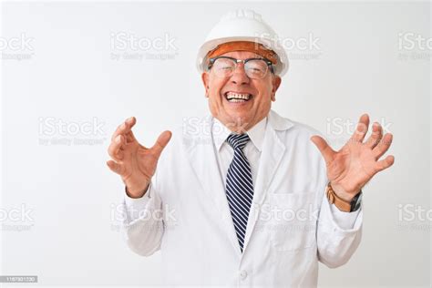 외투와 헬멧을 쓰고 있는 선임 회색 머리의 엔지니어 남자가 팔을 들고 눈을 감고 흥분을 일으키며 성공을 축하하는 고립된 흰색 배경 위에 있습니다 우승자 컨셉 건축가에 대한