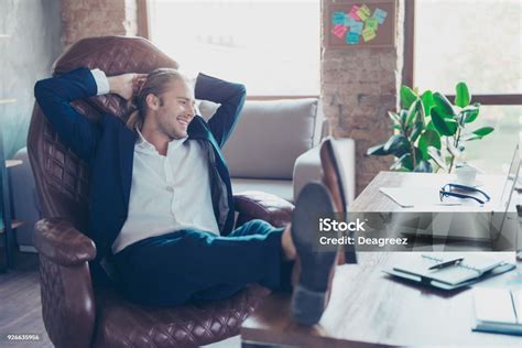 매력적인 웃는 행복 한 이사 직장에서 자신의 바탕 화면에 앉아 테이블에 다리를 퍼 팅 머리 뒤에 손을 잡고 휴식 시간을 즐기고 영화를 보고의 초상화 경영자에 대한 스톡 사진