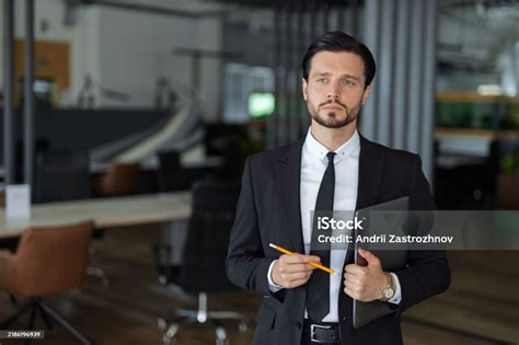 양복을 입은 남자가 연필과 서류 가방을 들고 있다 그는 의자와 책상이 있는 방에 서 있다 2에 대한 스톡 사진 및 기타 이미지 2 30 34세 Brand Name