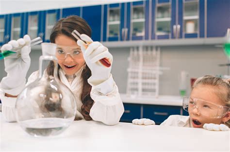 실험실 코트에서 두 작은 아이 학교 실험실에서 화학 학습 실험실 또는 화학 내각에 있는 실험을 만드는 방어적 인 유리에 있는 젊은 과학자 실험에 대 한 재료를 공부 위험한