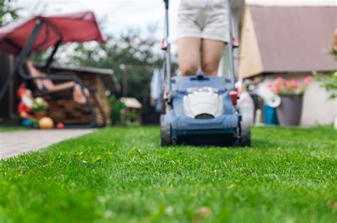 잔디 깎는 기계를 사용하여 정원에서 잔디를 자르는 사람 잔디 깎는 기계는 큰 바퀴가 달린 견고한 디자인을 가지고 있으며 앞으로 밀려나고 있습니다 배경에는 몇 가지 정원