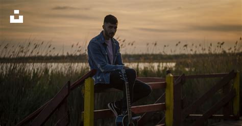 파란색 데님 재킷과 검은 바지를 입은 남자가 낮 동안 갈색 나무 울타리에 앉아 있다 사진 Unsplash의 무료 사람의 이미지