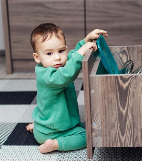 Niño pequeño abre los cajones de la cocina para jugar con los utensilios de cocina dentro bebé