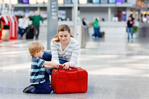 공항에서 젊은 어머니와 어린 유아 소년 아들 가족이 비행기를 기다리고 있습니다 비행기로 휴가를 보내는 어린이와 여성 터미널 실내에서 가방을 들고 있는 아들과 엄마 공항에