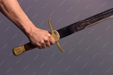 Premium Photo Cropped Hand Of Man Holding Sword Against Gray Background