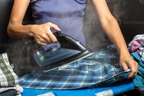 Woman Is Ironing Clean Clothes With A Hot Iron And Steam Neatly Folded Shirts Lie Nearby