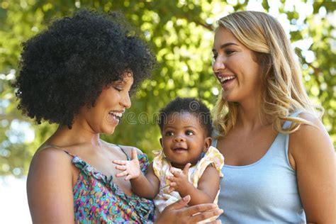 Loving Same Sex Female Couple Or Friends Cuddling Baby Outdoors In